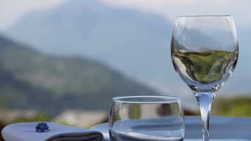 Um copo de vinho branco e um copo de água sobre uma mesa, com vista para montanhas ao fundo.