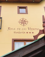 Um edifício com uma placa que diz 'Rosa de los Vientos Hostería' e um símbolo de bússola acima do texto.