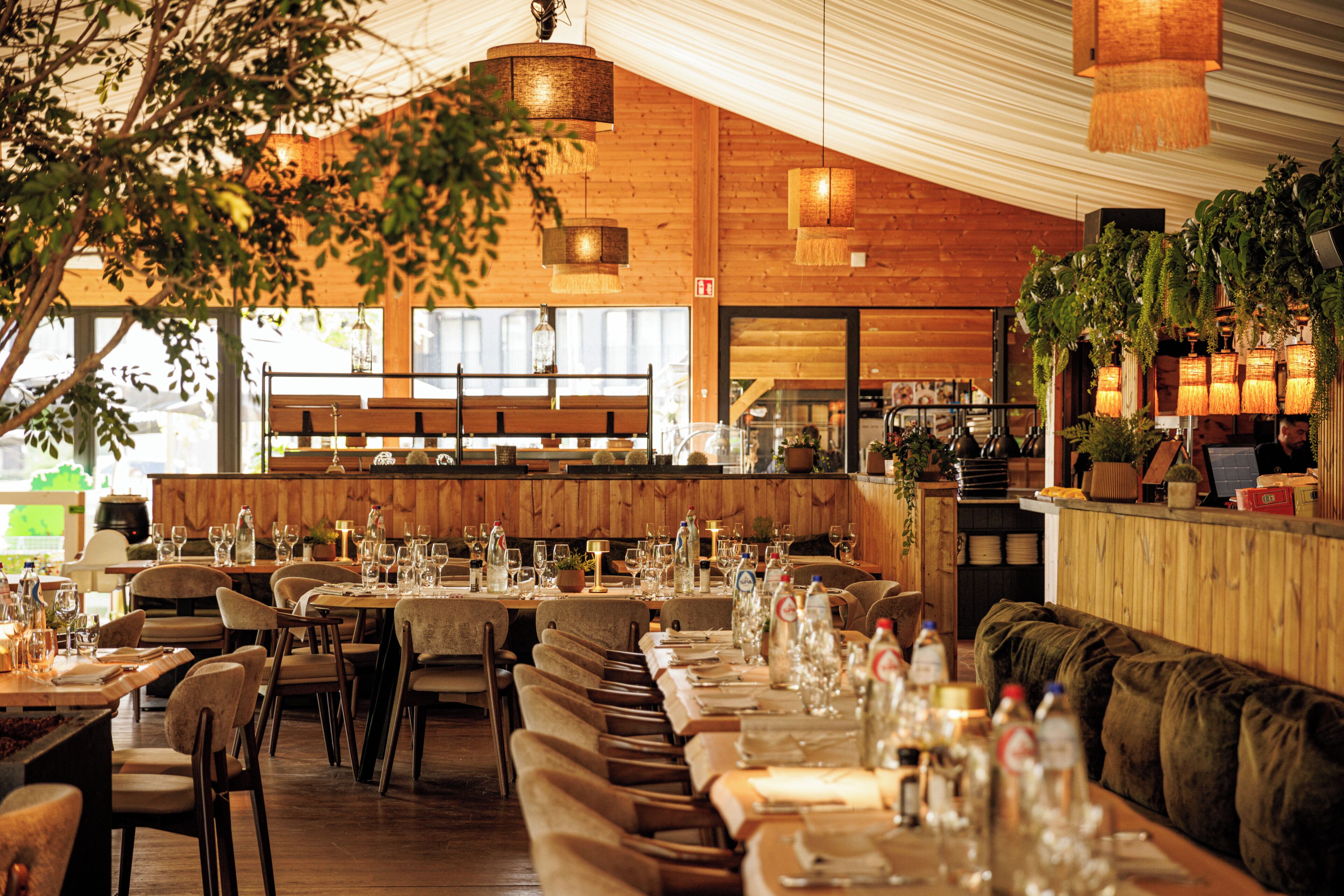 Restaurante com interiores em madeira, várias mesas para refeições e luminárias pendentes.