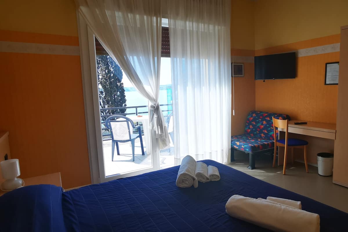 Quarto de hotel com cama, escrivaninha, cadeira e vista para o exterior.