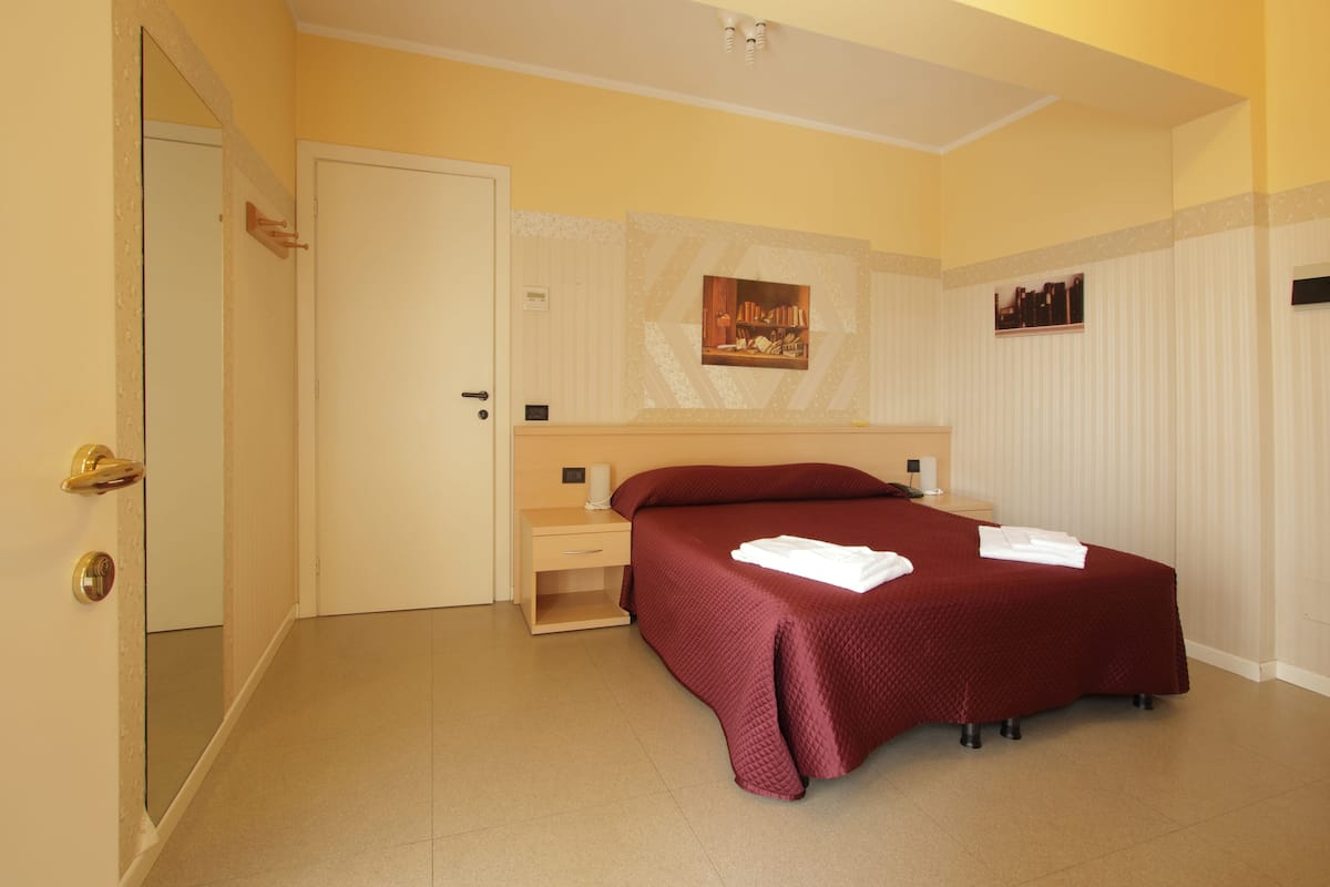 Quarto de hotel com cama, mesa de cabeceira, espelho e porta.