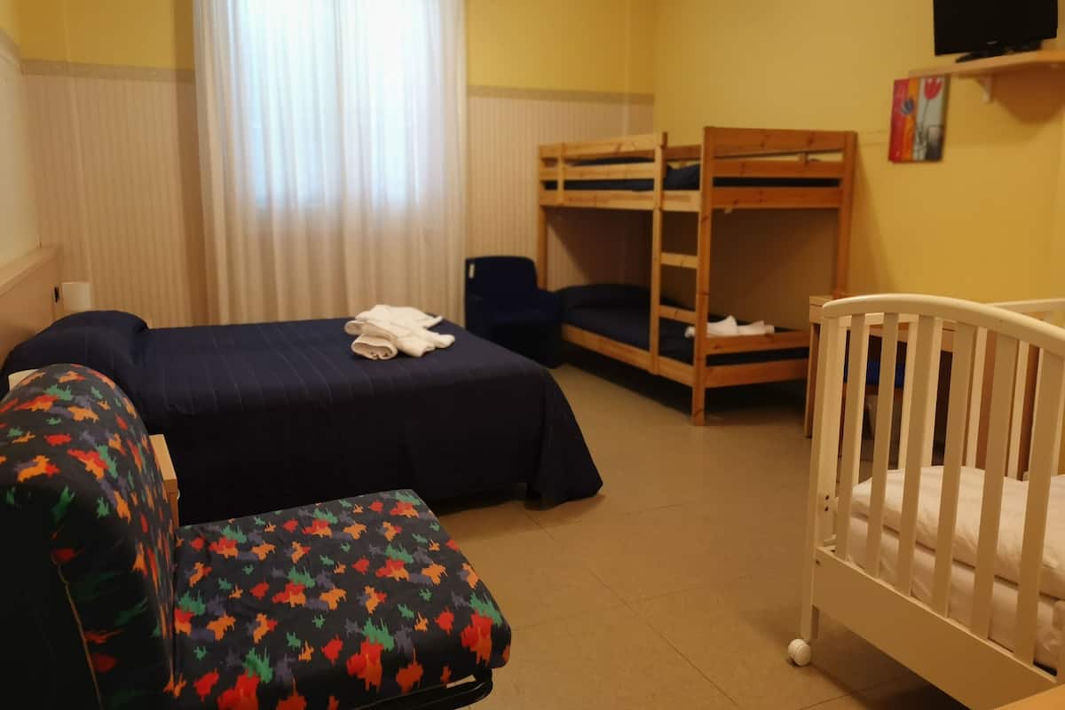 Quarto de hotel com duas camas, um berço, uma cadeira e uma televisão numa prateleira.