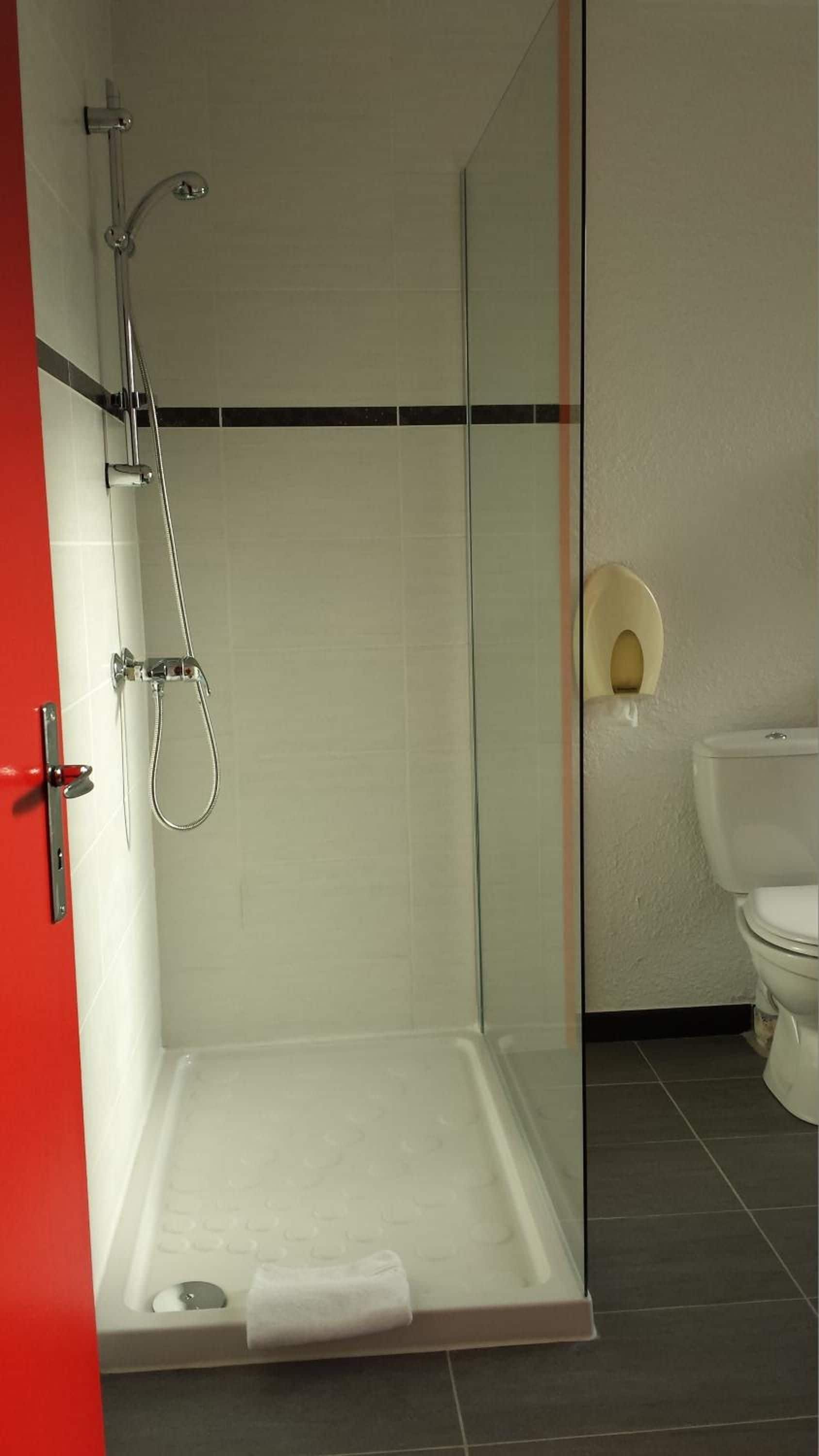 Casa de banho moderna com chuveiro de vidro, sanita e porta vermelha.