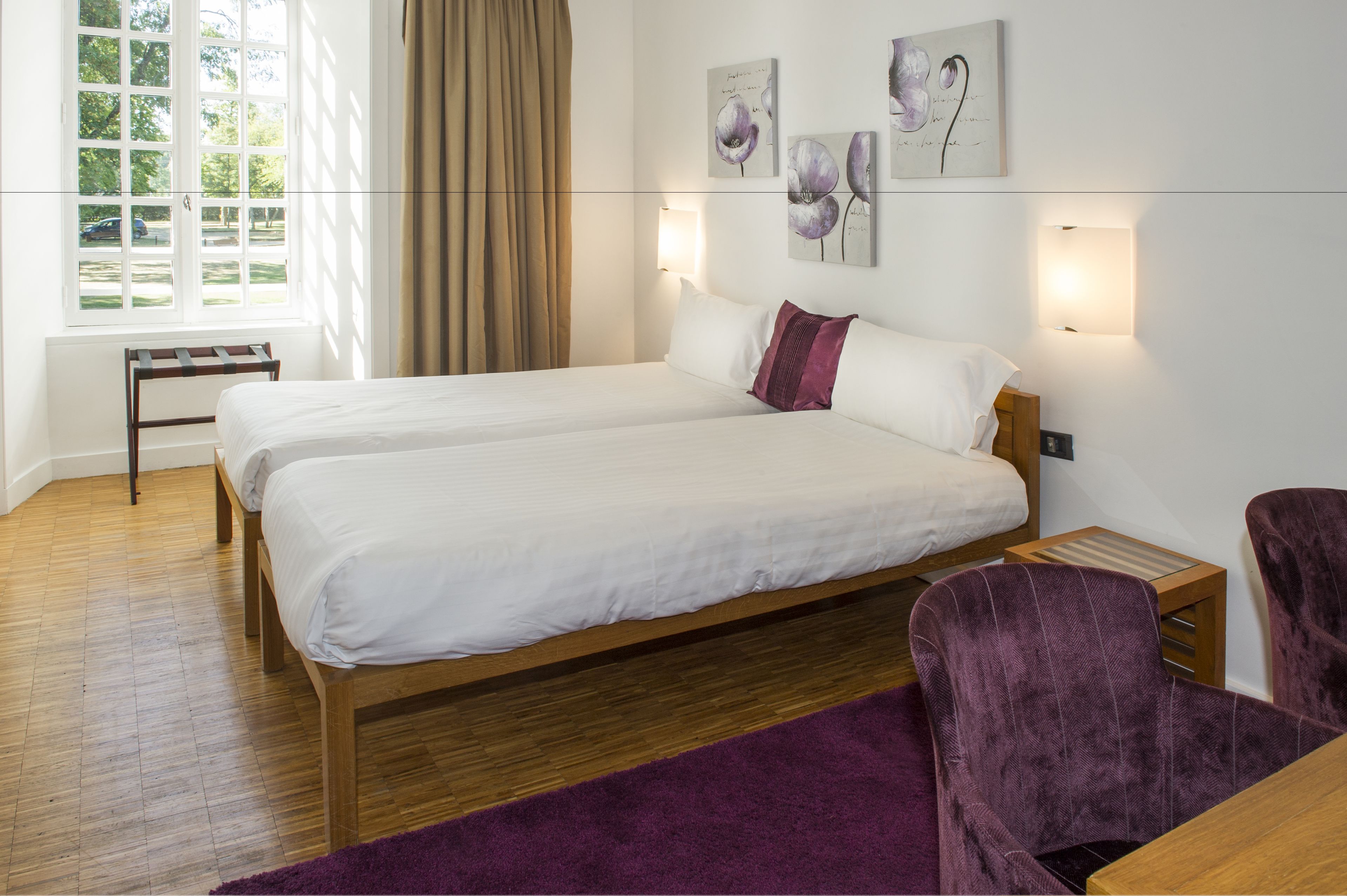 Quarto de hotel com duas camas, piso de madeira, tapete roxo e obras de arte na parede.