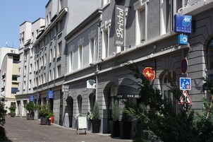Fachada de hotel com placas indicando Bristol Hotel, um aviso de proibido estacionar e um sinal de travessia de pedestres.