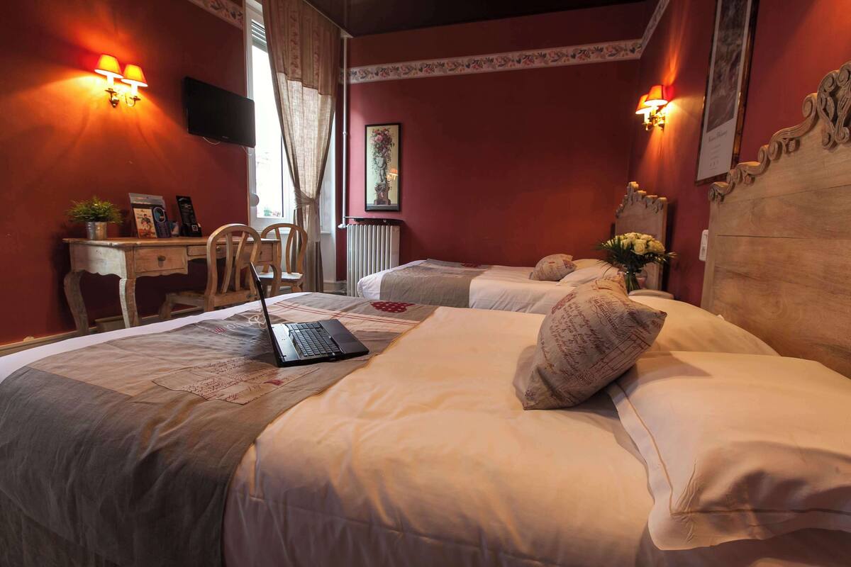 Quarto de hotel com duas camas, uma escrivaninha com um laptop, uma cadeira e uma televisão na parede.