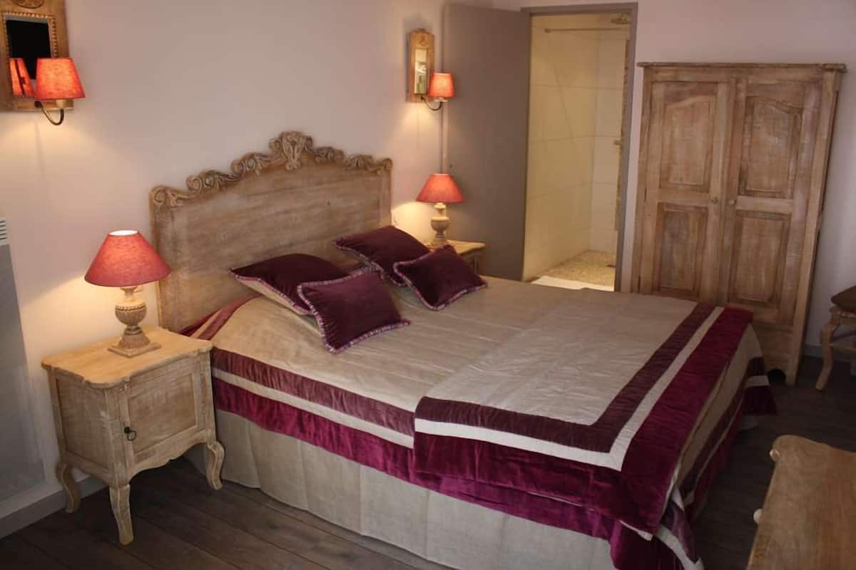 Quarto com uma cama grande, duas mesas de cabeceira com abajures, um guarda-roupa de madeira e um espelho na parede.