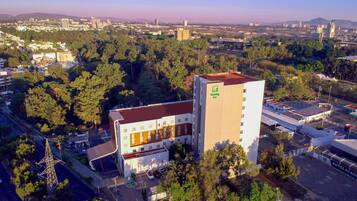 Um hotel Holiday Inn rodeado por árvores e edifícios, com um parque de estacionamento e uma rua à vista.