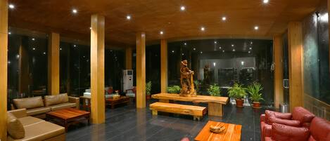 Um hall amplo com sofás de couro, mesas de madeira e plantas em vasos.