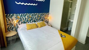 Quarto de hotel com cama, cabeceira estampada com padrão de folha, mesa de cabeceira e uma pequena mesa redonda.