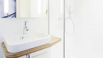 Uma casa de banho moderna com uma pia branca, um espelho e um chuveiro com parede de vidro.