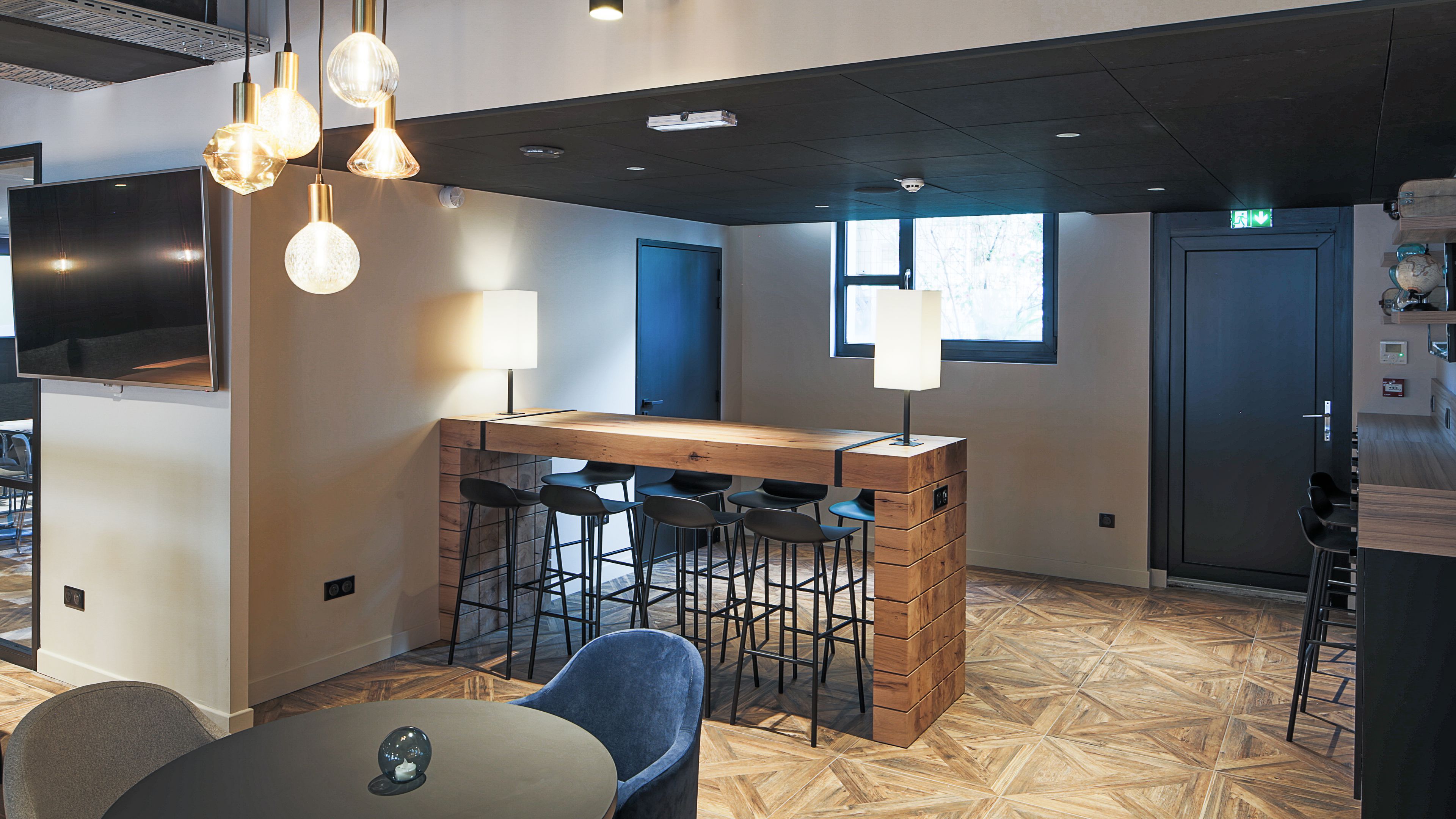 Uma área de bar moderna com balcão de madeira, banquetas e iluminação pendente.