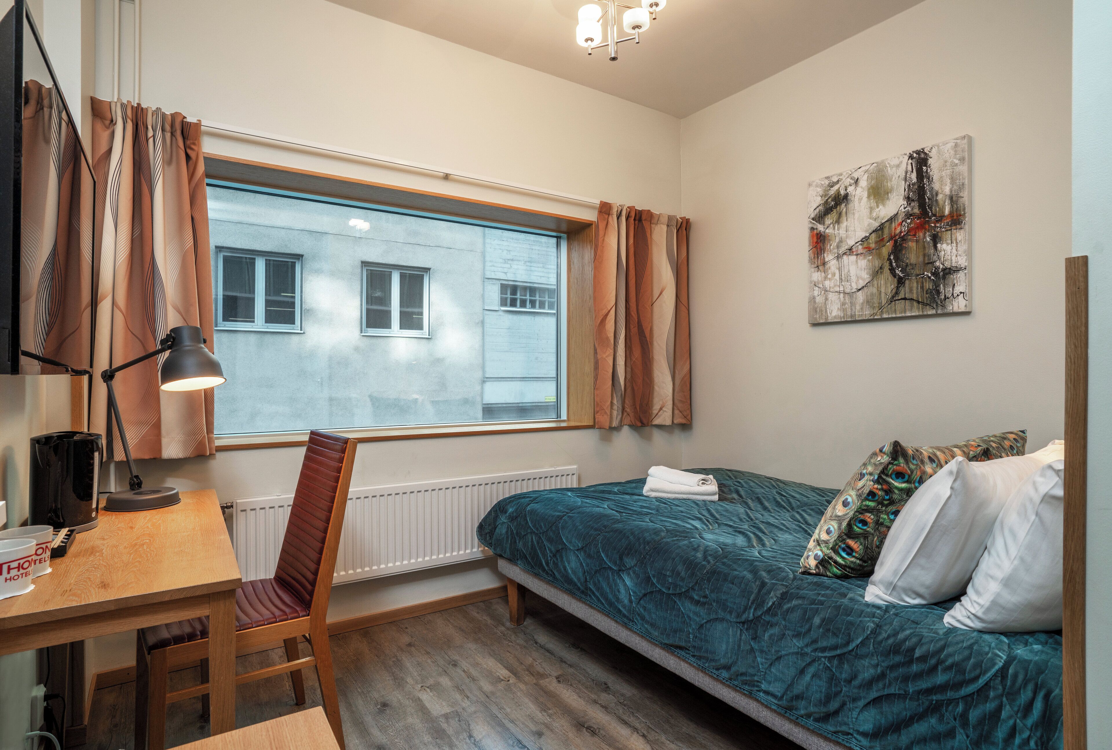 Quarto com cama, escrivaninha, cadeira, janela e radiador.