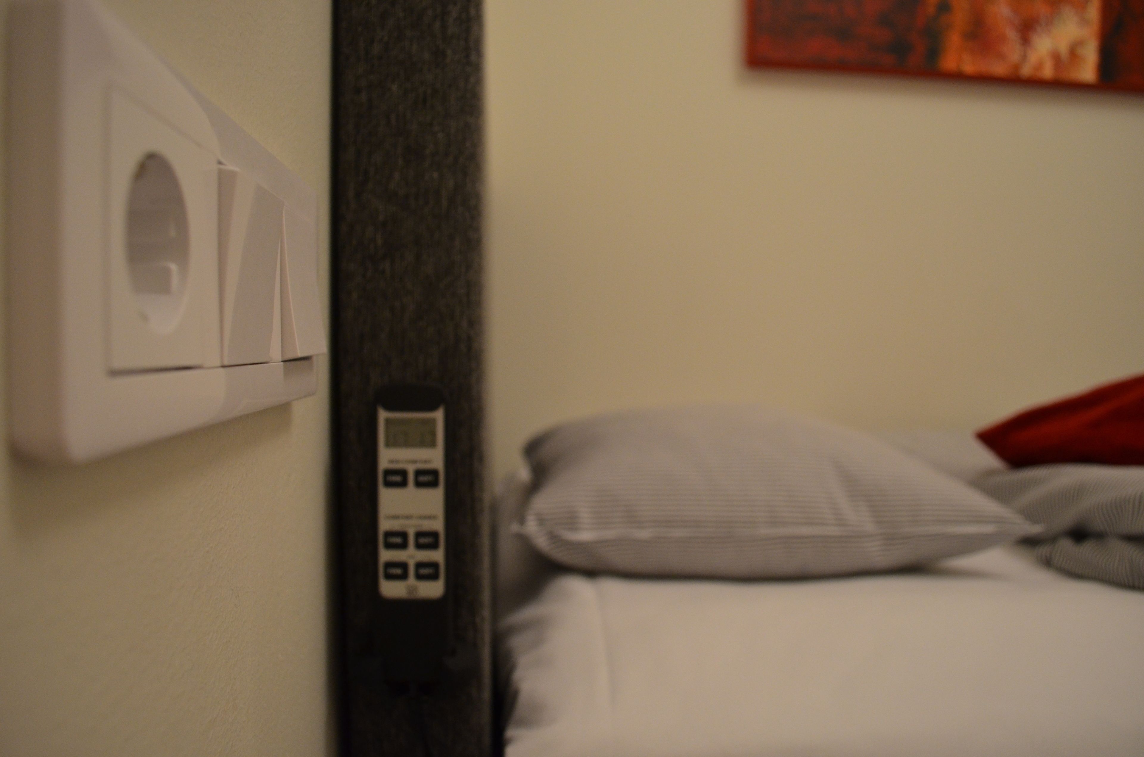 Quarto de hotel com painel de controle, cama com almofadas e unidade de ar condicionado na parede.