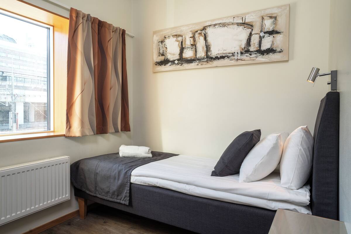 Quarto com cama, radiador, janela com cortinas e um quadro na parede.