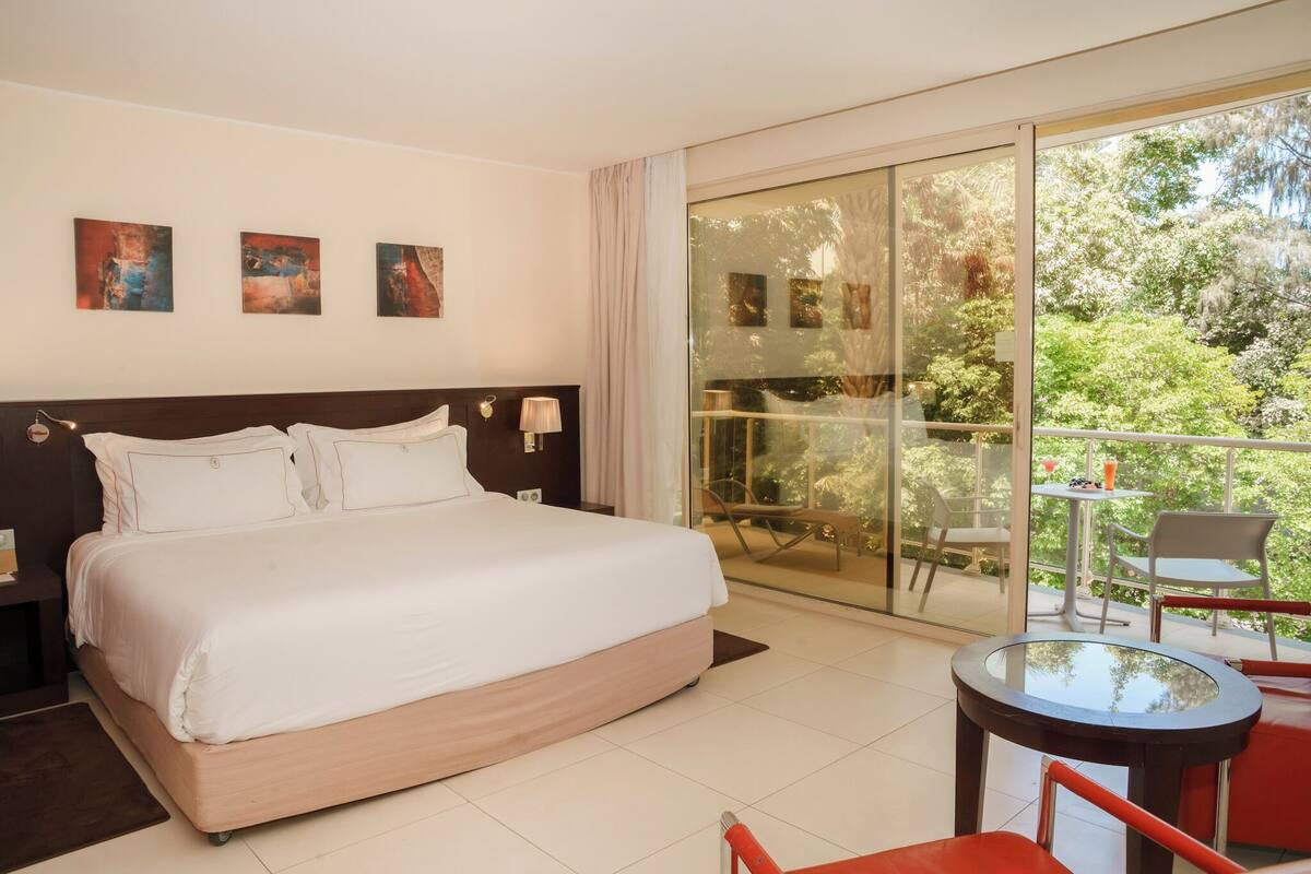 Quarto de hotel com uma cama grande, porta de vidro que dá para uma varanda com área de estar ao ar livre.