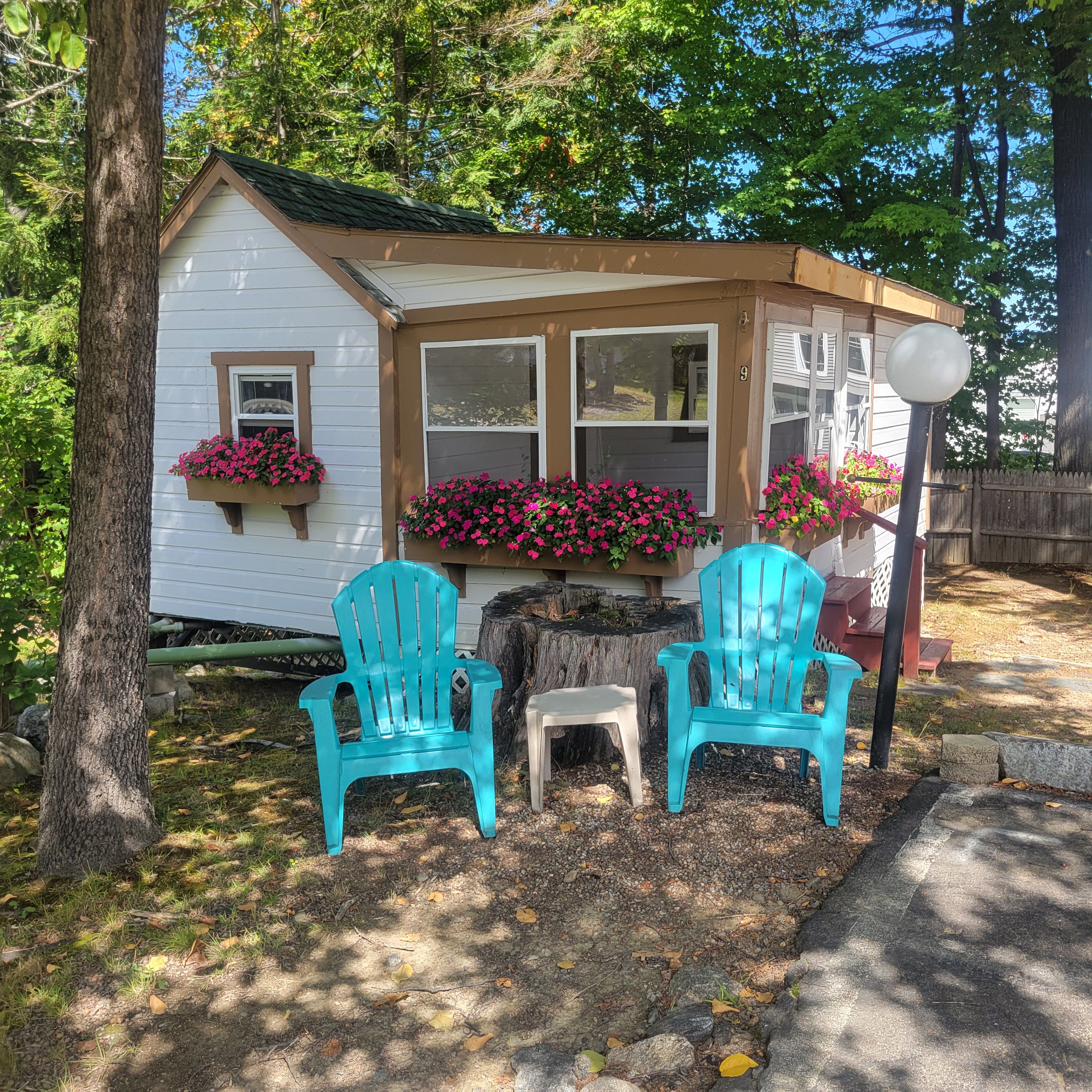 Uma cabana pequena com duas cadeiras Adirondack e jardineiras nas janelas.