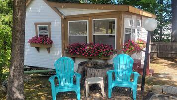 Uma cabana pequena com duas cadeiras Adirondack e jardineiras nas janelas.