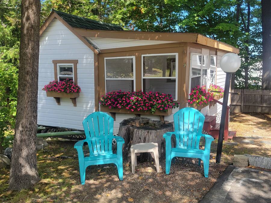Uma cabana pequena com duas cadeiras Adirondack e jardineiras nas janelas.