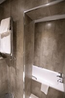 Uma casa de banho moderna com chuveiro separado por vidro e banheira branca.