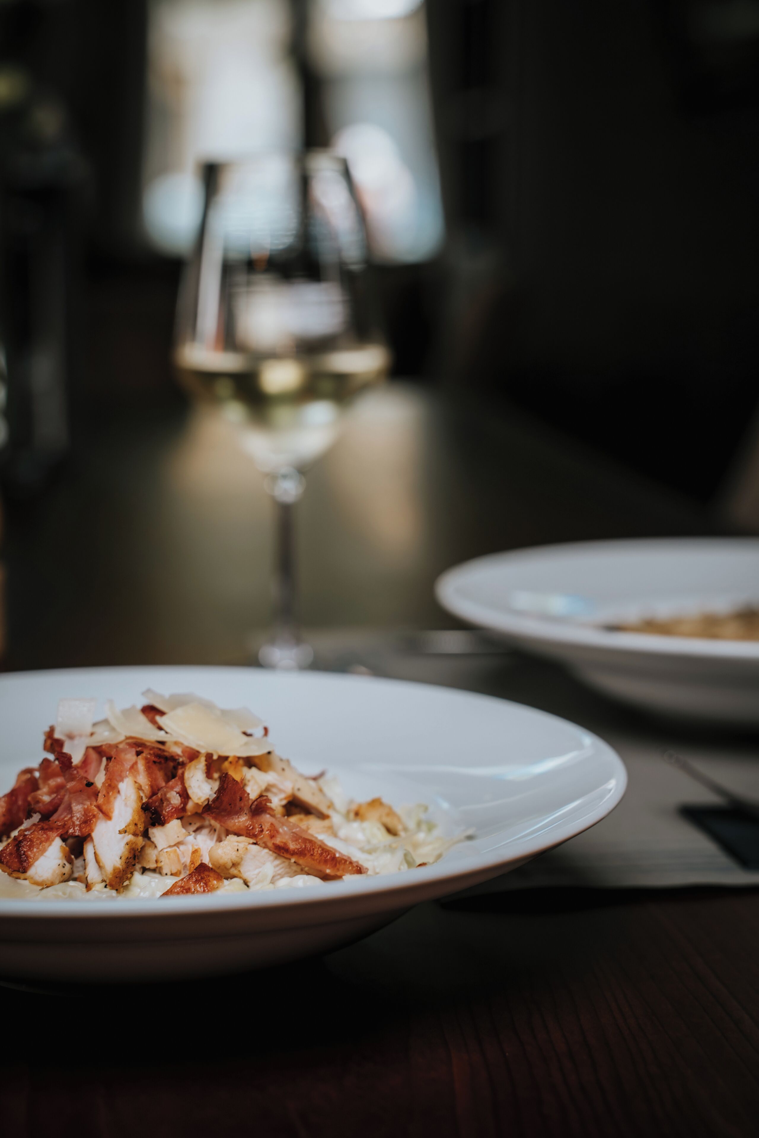 Uma mesa de jantar com pratos de comida e um copo de vinho branco.