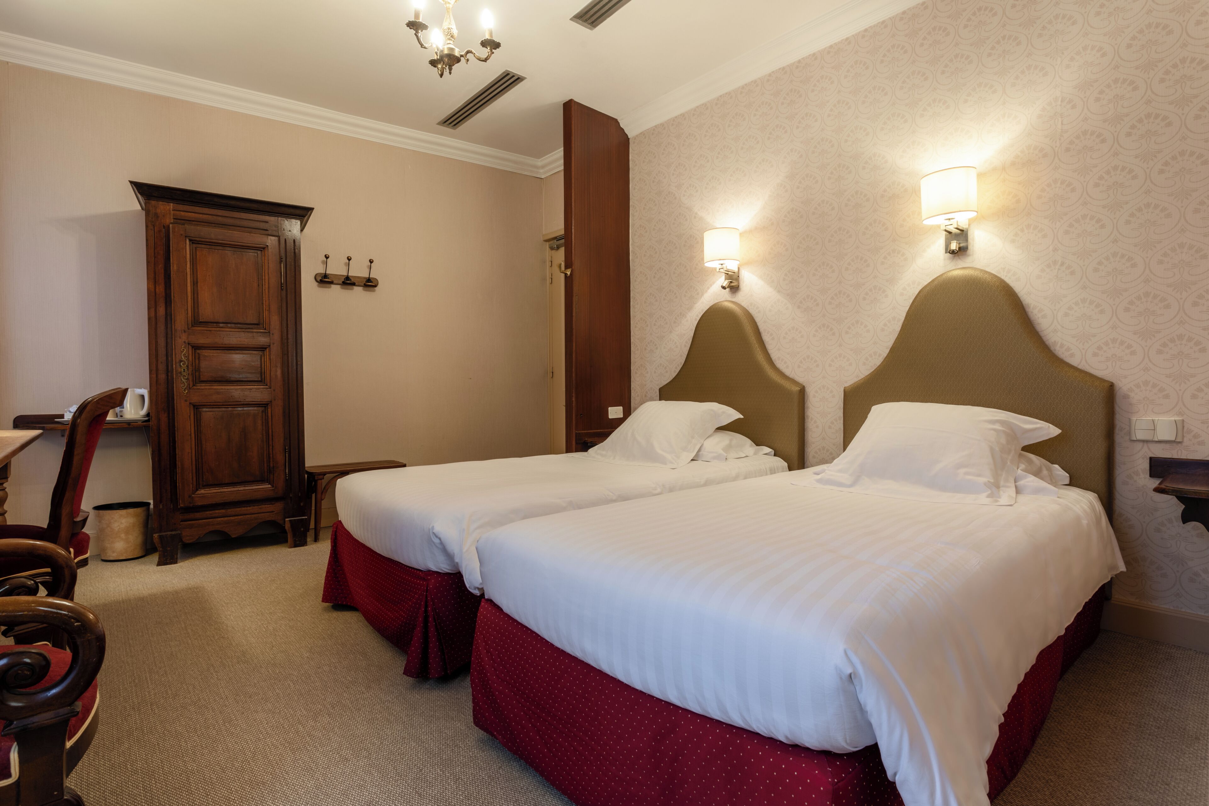 Quarto de hotel com duas camas, um guarda-roupa de madeira, uma escrivaninha e uma cadeira.