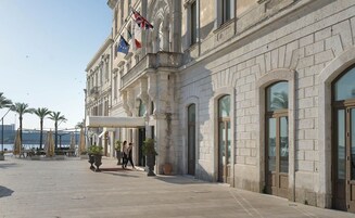 Um edifício histórico com fachada clássica, grandes janelas e área de entrada coberta.