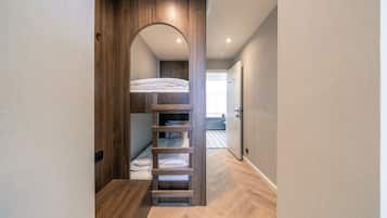 Corredor estreito com escada de madeira que leva a um quarto no mezanino com beliche.