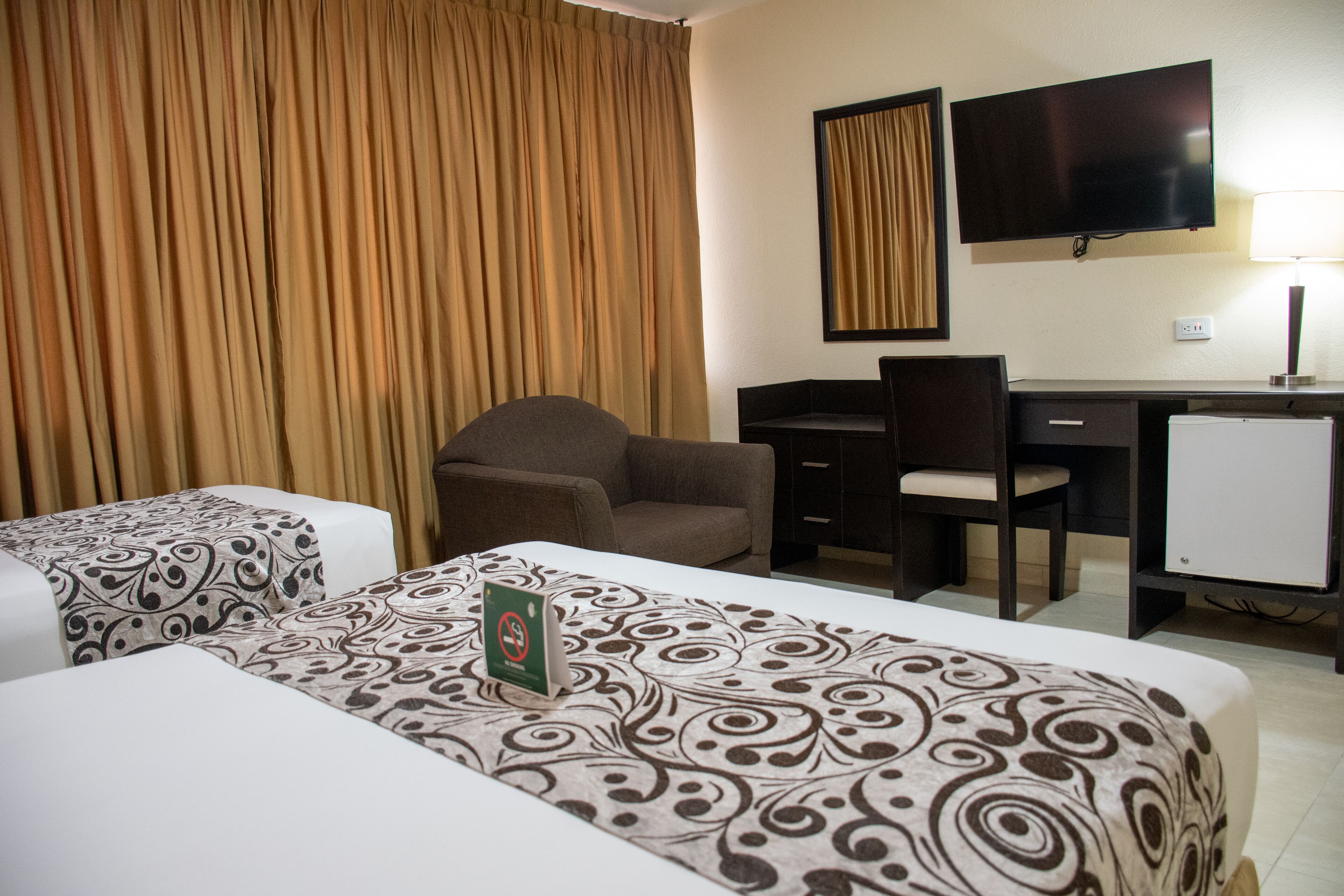 Quarto de hotel com duas camas, uma escrivaninha, uma cadeira, uma televisão e cortina.