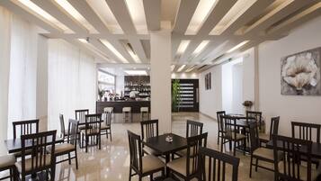 Uma área de jantar moderna com mesas e cadeiras de madeira, um bar ao fundo e um grande quadro abstrato na parede.