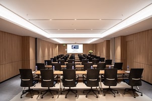 Uma sala de conferências com várias mesas, cadeiras e uma tela grande na frente.