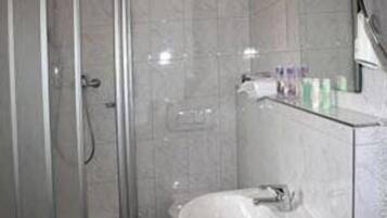 Uma casa de banho com cabine de chuveiro em vidro, lavatório branco e espelho sobre o lavatório.