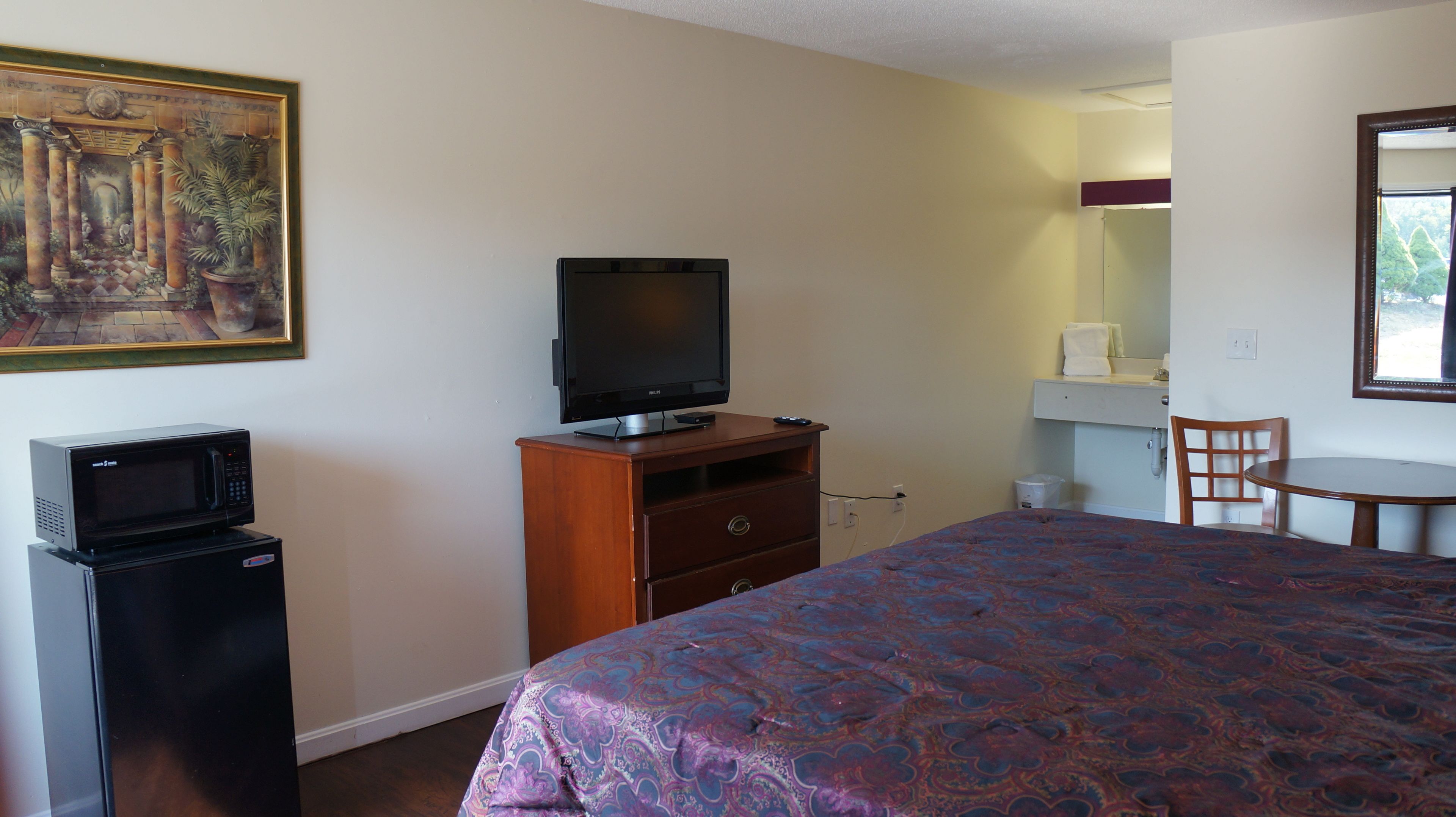 Quarto de hotel com cama, televisão, micro-ondas, mesa pequena e cadeira.