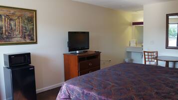 Quarto de hotel com cama, televisão, micro-ondas, mesa pequena e cadeira.