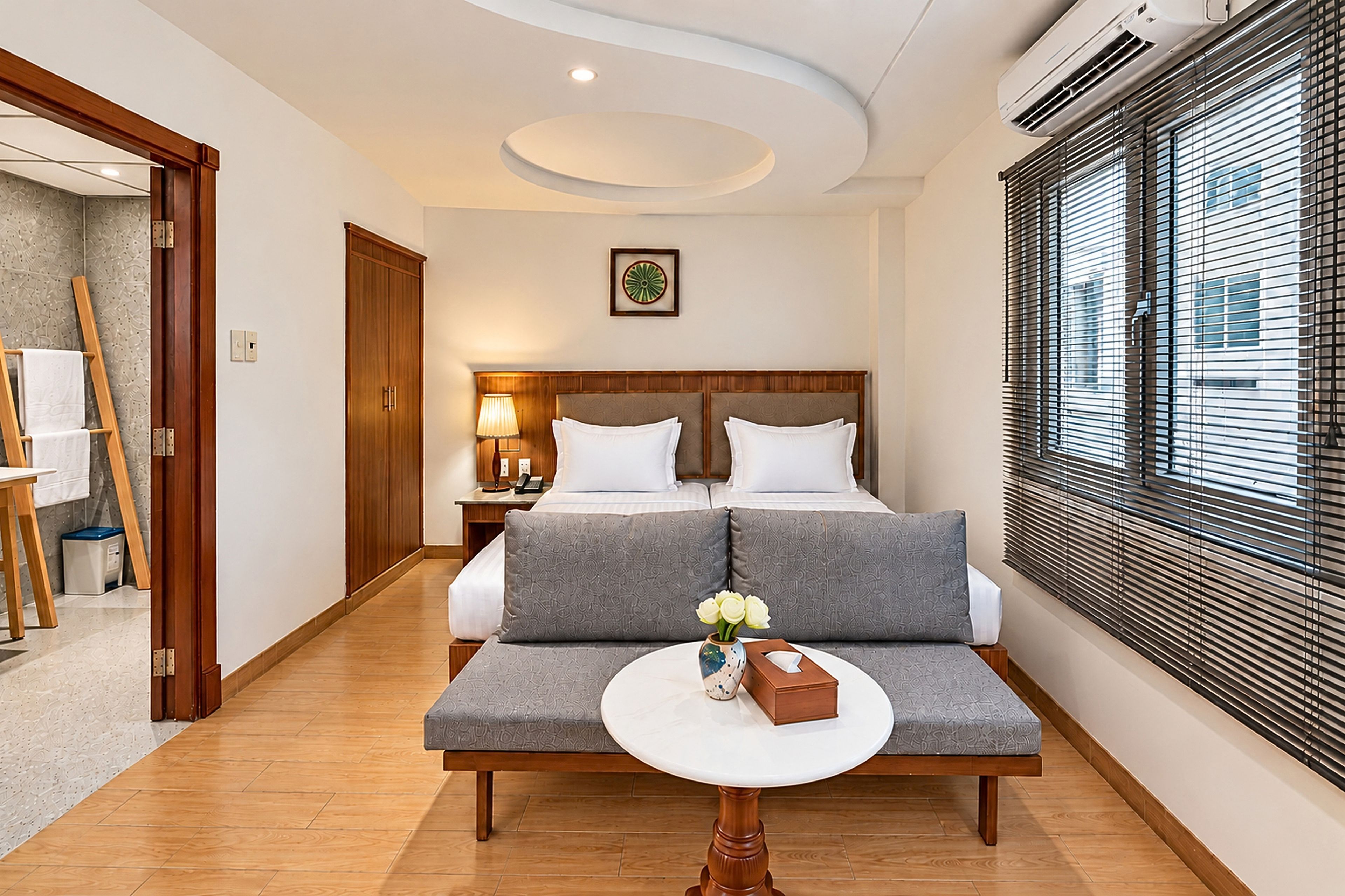 Quarto de hotel com uma cama, um sofá, uma mesinha e uma janela com persianas.