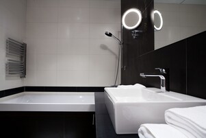 Uma casa de banho moderna com uma banheira grande e branca, uma pia separada e um espelho iluminado por luzes circulares.