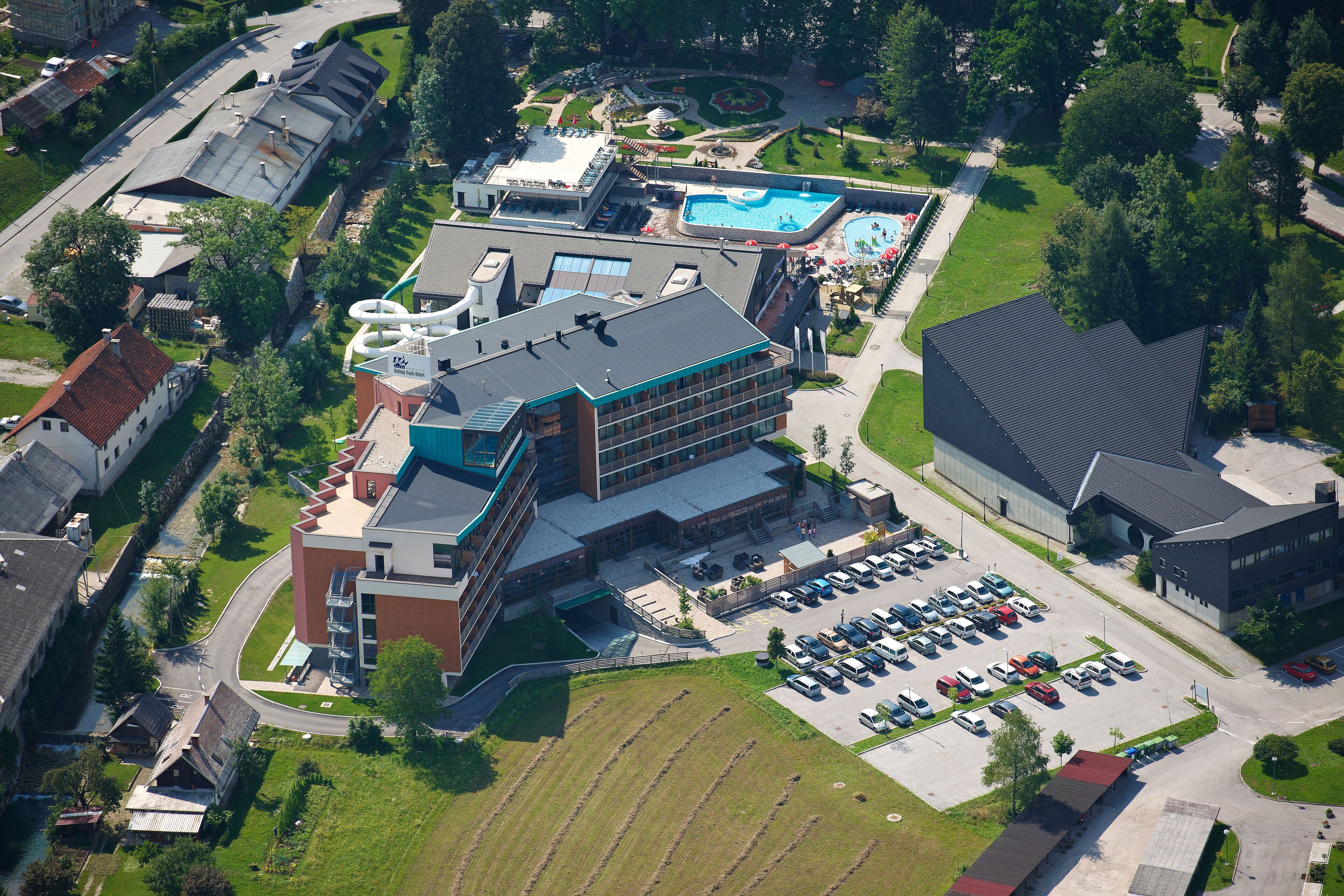 Vista aérea de um hotel moderno com piscina, estacionamento e áreas ajardinadas.