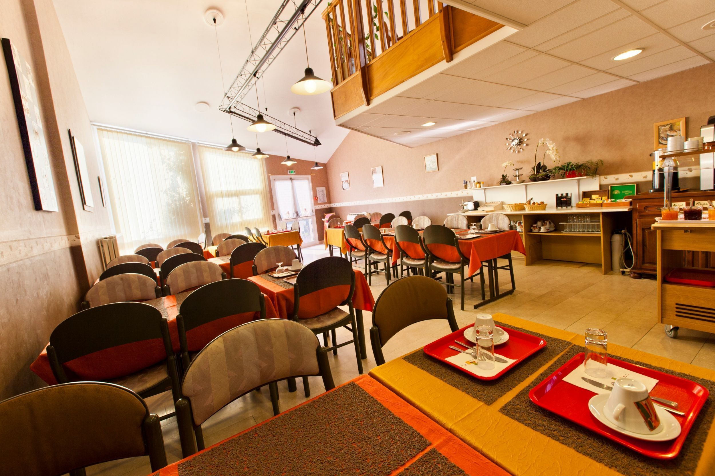Um restaurante com várias mesas e cadeiras, área de cozinha e teto alto com vigas aparentes.