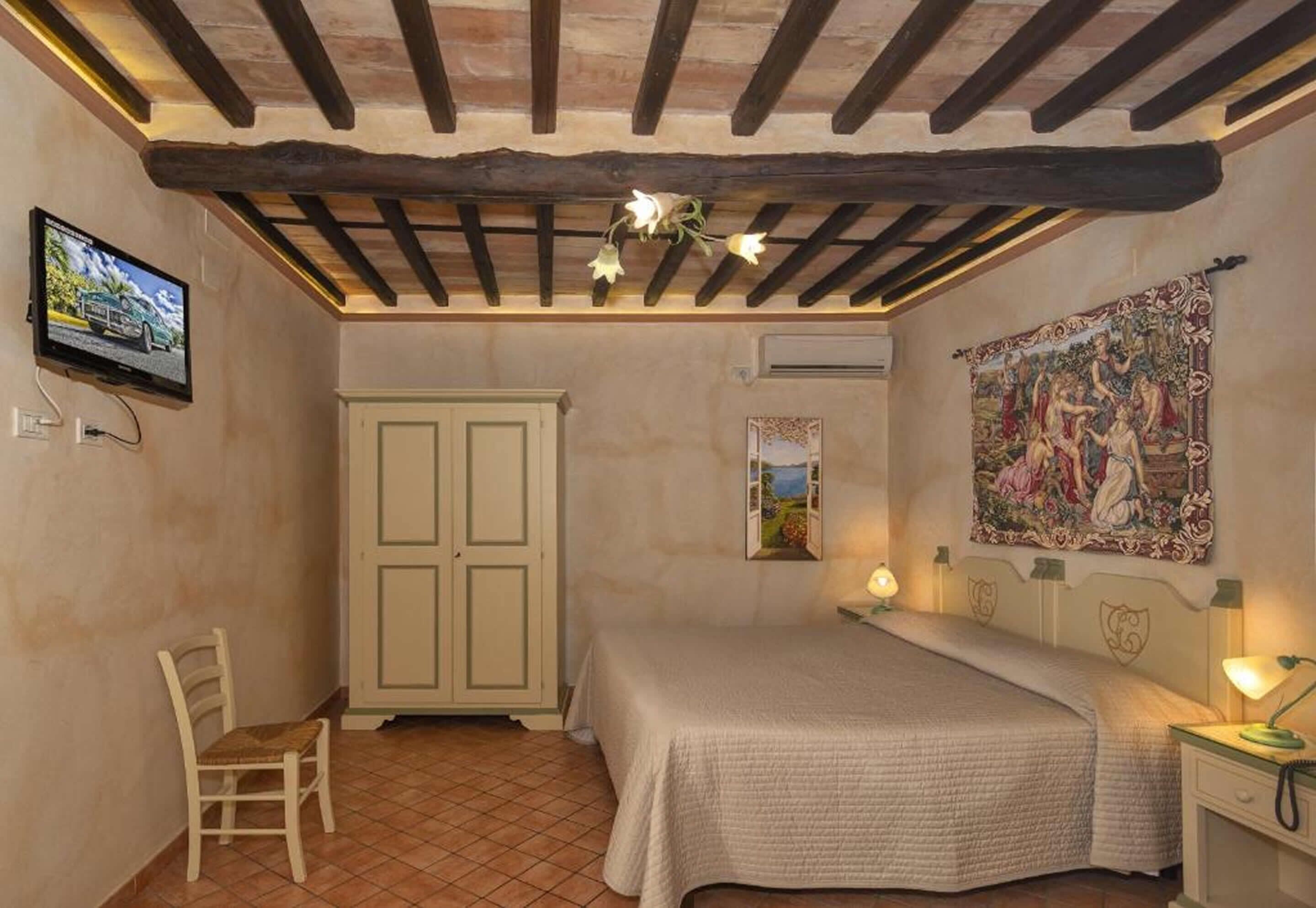 Quarto com cama, cadeira, televisão, armário e tapeçaria.