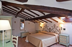 Quarto com teto de madeira, cama com cabeceira, mesas de cabeceira, uma cadeira, cômoda e espelho.