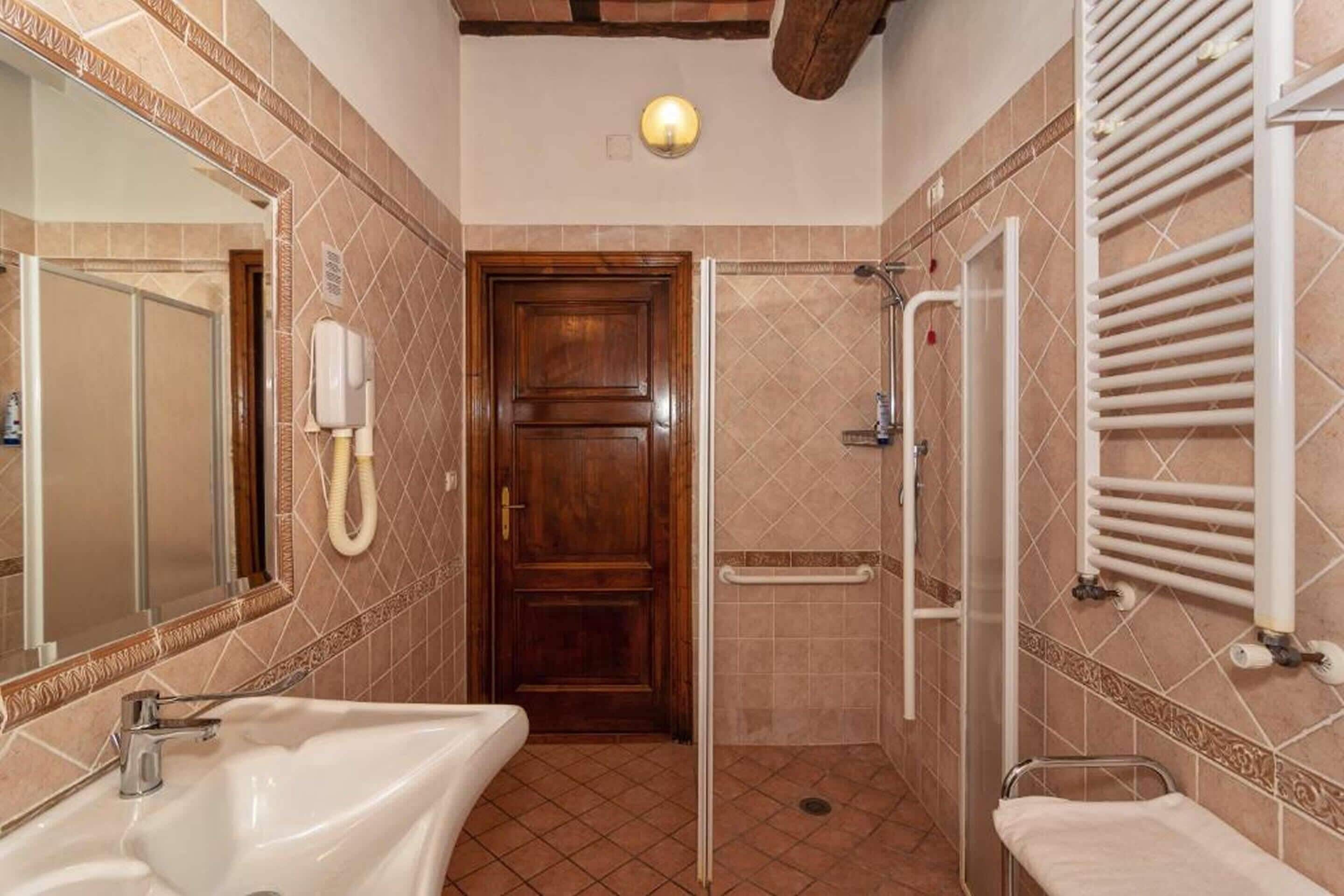 Casa de banho com lavatório, espelho, chuveiro e porta-toalhas.
