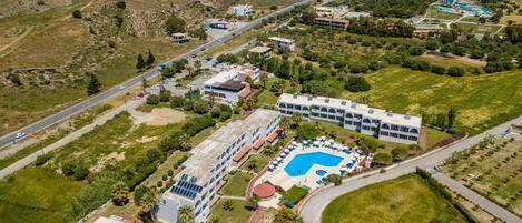 Vista aérea de um resort com vários edifícios, uma piscina e vegetação ao redor.