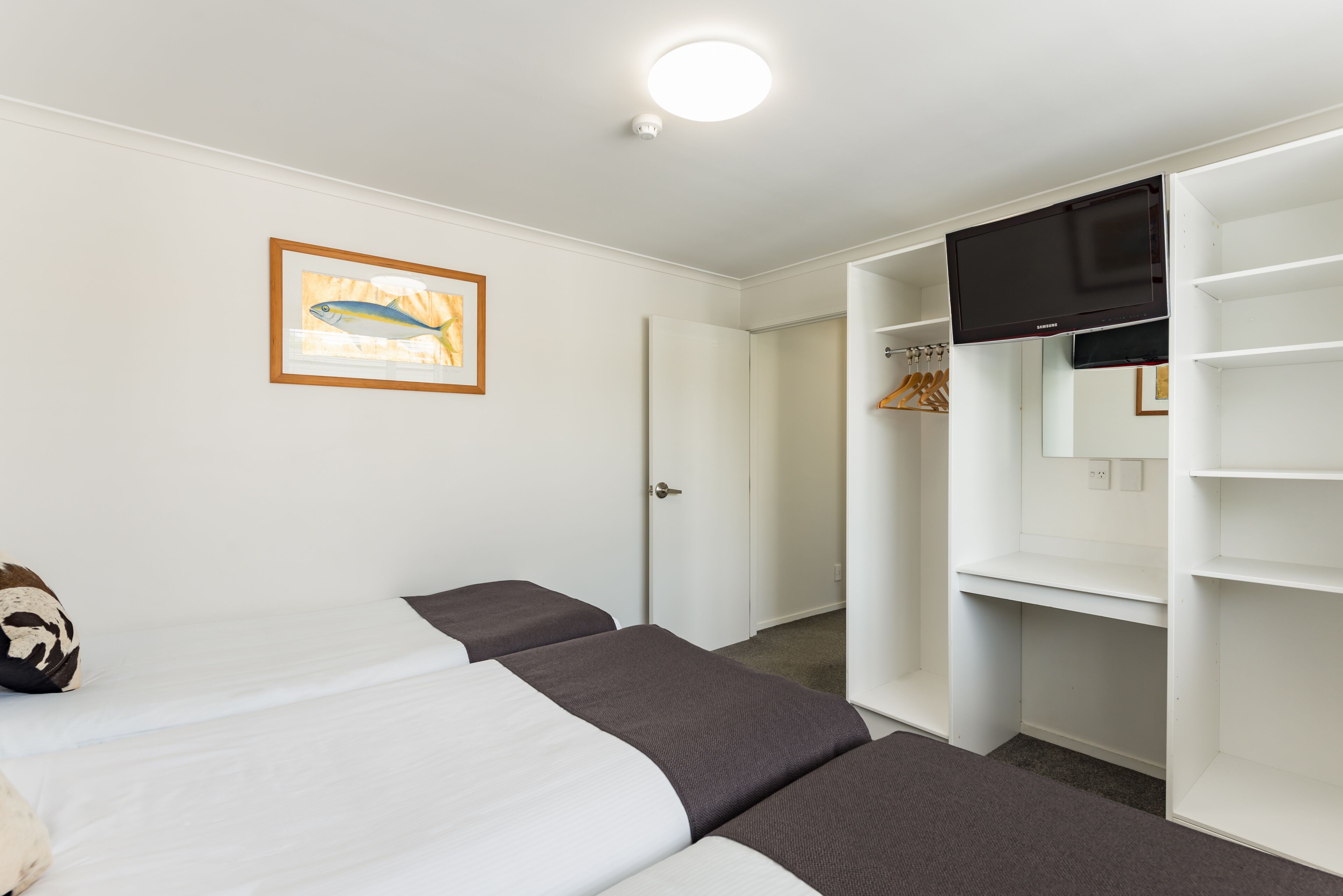 Quarto de hotel com cama, guarda-roupa, televisão de tela plana e um quadro na parede.