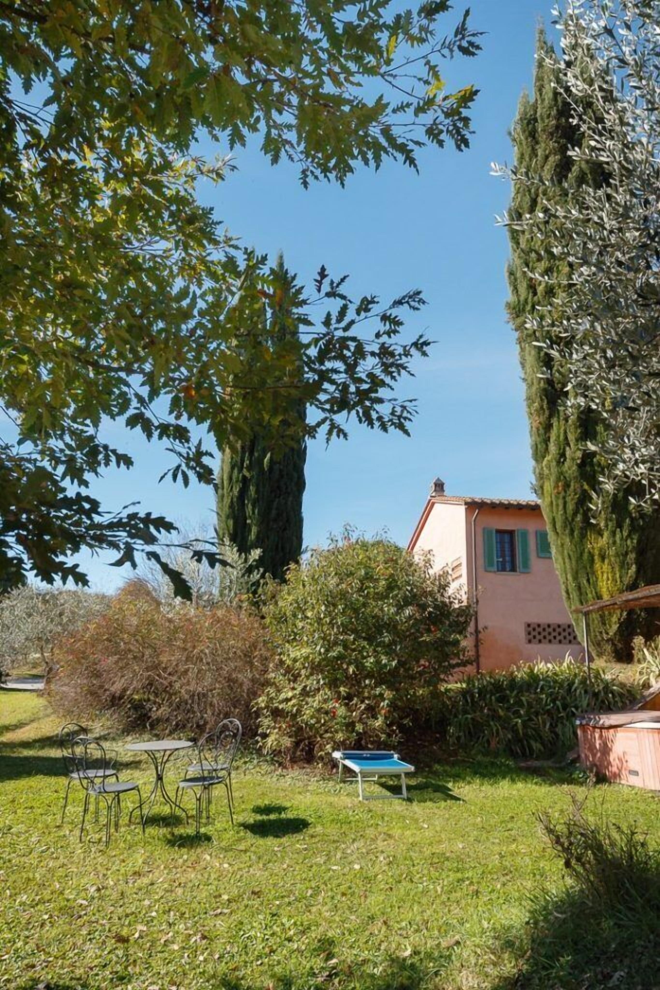 Um jardim com uma mesa e cadeiras, uma mesa de tênis de azul e uma árvore alta.