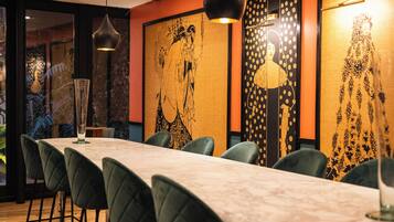 Uma sala de jantar com uma mesa comprida, cadeiras estofadas verdes e painéis decorativos na parede.