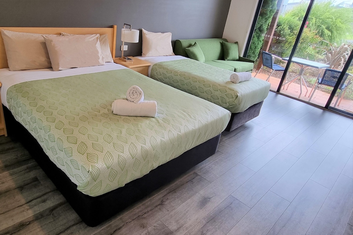 Quarto de hotel com uma cama grande, uma cama menor, um sofá e uma área de jantar com cadeiras.