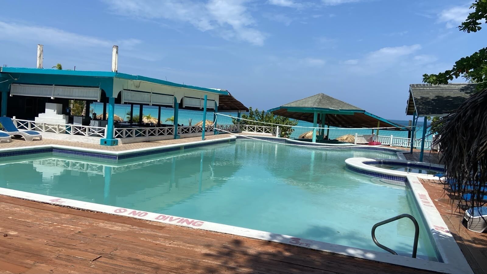 Uma piscina com um aviso de 'Não Mergulhar', espreguiçadeiras e uma área de estar coberta.