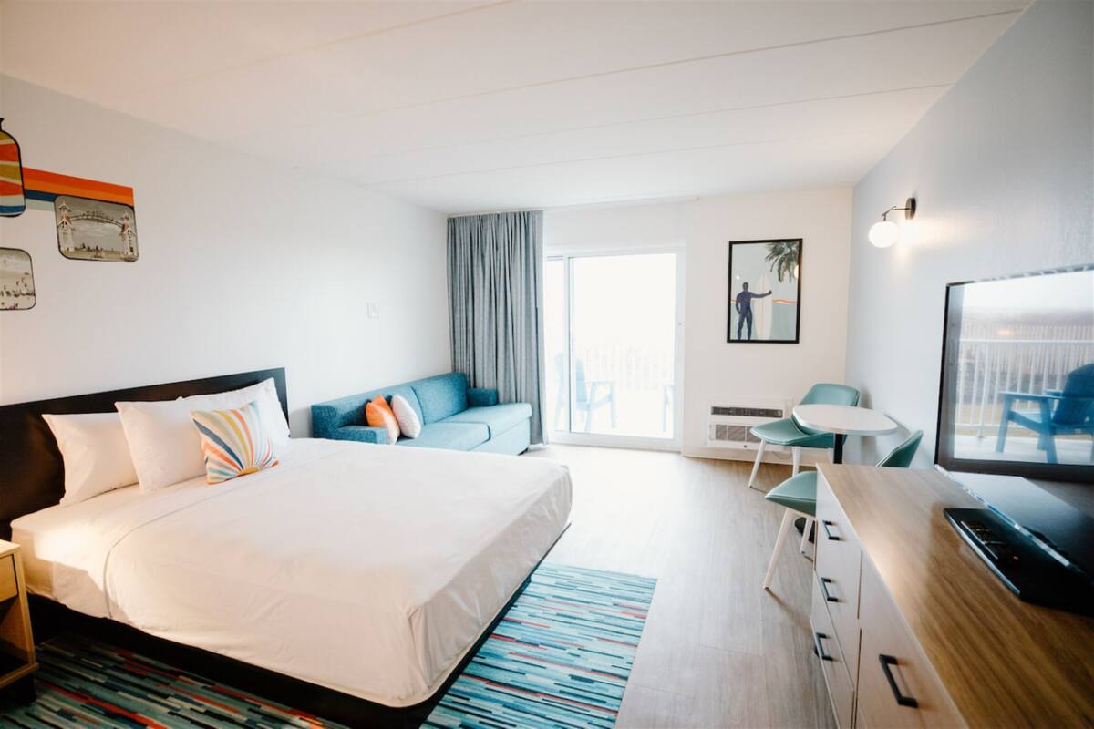 Quarto de hotel moderno com uma cama grande, um sofá, uma escrivaninha e uma televisão.