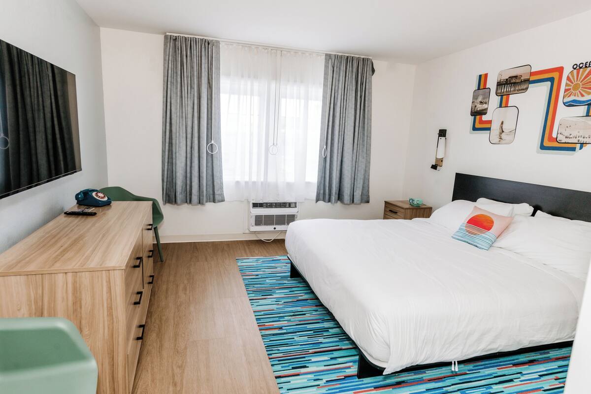 Quarto de hotel moderno com uma cama grande, uma escrivaninha e uma TV.