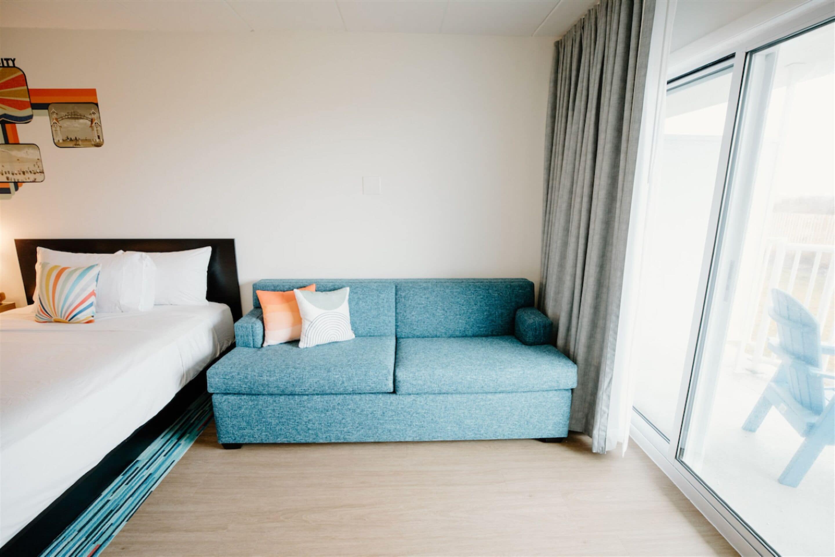 Quarto de hotel com cama, sofá azul e uma janela grande.